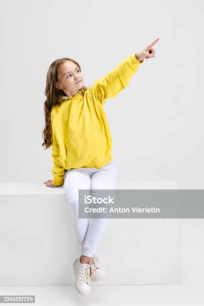 흰색 배경 위에 고립 된 곳을 가리키는 노란색 스웨터를 입은 아름다운 소녀의 전체 길이 초상화 10 11세에 대한 스톡 사진 및 기타 이미지 Istock