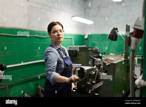 Portrait Of Confident Attractive Female Engineer In Safety Goggles Using Manual Lathe While