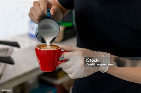 아름다운 라떼 카푸치노 아트 로제타 패턴을 만드는 커피 컵에 찐 우유를 붓는 바리스타를 닫습니다 라떼 아트를 만들기 위해 레드 커피 컵에 따뜻한 우유를 붓는 바리스타 손을