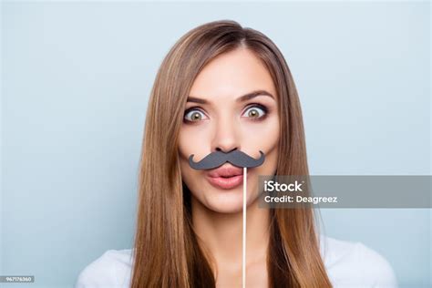 스틱 카메라 보고 활짝 열려 눈 회색 배경에 고립 메기 입술에 검은 판지 콧수염을 들고 재미 있는 어리석은 여자의 초상화를 닫습니다 여자에 대한 스톡 사진 및 기타 이미지