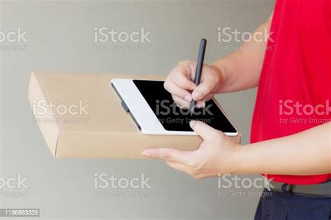 우편 배달 부는 갈색의 배경에 소포 상자를 들고 서 영수증에 서명 하는 태블릿을 건네 섰다 과로에 대한 스톡 사진 및 기타