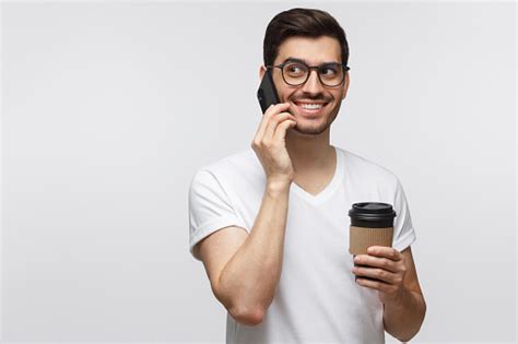 캐주얼 흰색 티셔츠와 안경에 잘 생긴 젊은 남자의 초상화 전화에 이야기하고 테이크 아웃 커피를 들고 T 셔츠에 대한 스톡 사진
