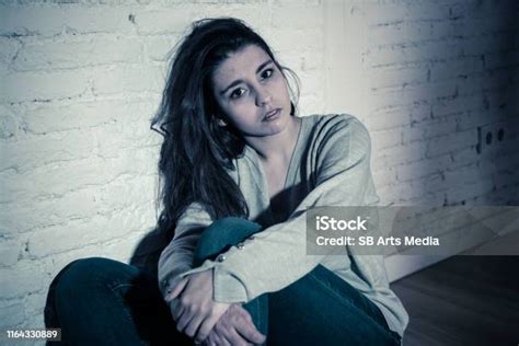 비참하고 외롭고 절망적이며 슬픈 젊은 라틴 여성의 초상화가 복사 공간과 우울한 빛을 가진 흰색 벽에 바닥에 앉아 있습니다 우울증과 정신 건강 개념에서 감정에 대한 스톡 사진