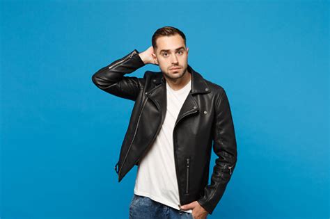 블랙 가죽 자 켓 흰색 T 셔츠에 잘생긴 세련 된 젊은 수염 남자 블루 벽 배경 스튜디오 초상화에 고립 된 카메라를 찾고 사람들은 진심으로 감정 라이프 스타일 개념입니다