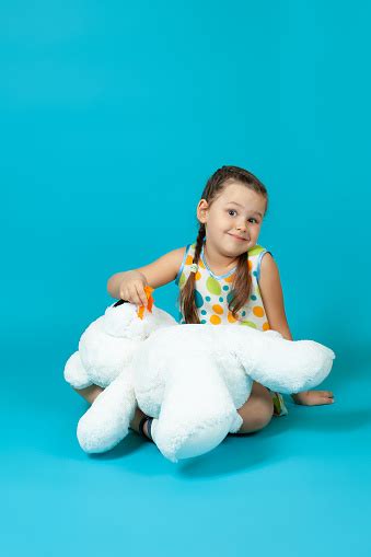 바닥에 다리를 꼬고 앉아 치과 의사를 재생 피그 테일과 소녀는 파란색 배경에 고립 된 흰색 테디 베어에서 아기 치아를 꺼내