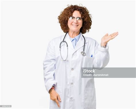 웃 고 쾌활 한 제시 하 고 카메라를 보고 손바닥으로 가리키는 격리 된 배경 위에 중간 어른 수석 의사 여자 가리키기에 대한 스톡 사진 및 기타 이미지 Istock