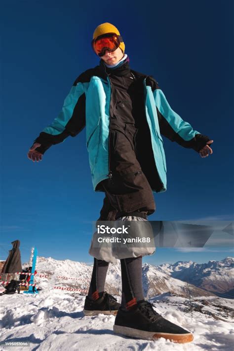 따뜻한 바람막이 모자를 쓰고 눈 덮인 산을 배경으로 서서 카메라를 바라보며 웃고 있는 매력적인 남자 추운 겨울의 개념 겨울에 대한 스톡 사진 및 기타 이미지 Istock