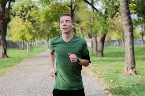 정신 건강 및 자기 관리 활동의 일환으로 공공 공원에서 야외에서 부드러운 일상 운동을하는 행복한 운동 중반 성인 남성 그는 운동복과 스마트 워치를 착용하고 조깅을하고