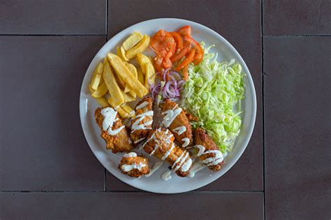 짙은 나무 테이블에 는 감자 튀김 녹색 샐러드 토마토를 곁들인 화이트 요거트 소스를 얹은 프라이드 치킨 윙의 세계 각국의 요리