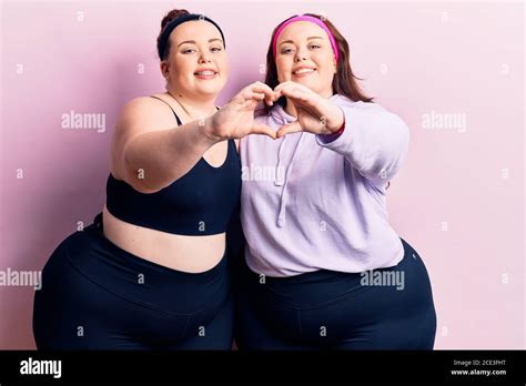 Young Plus Size Twins Wearing Sportswear Smiling In Love Doing Heart Symbol Shape With Hands
