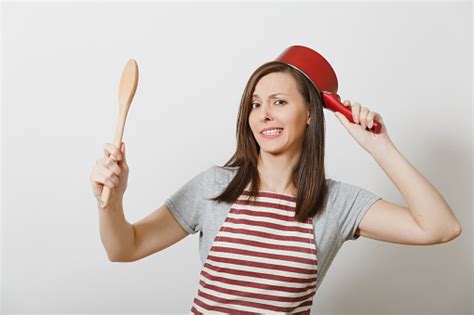 젊은 미소 스트라이프 앞치마에 미친 주부 회색 티셔츠 흰색 배경에 고립 아름 다운 재미 있는 정부 여 자가 머리 나무 숟가락에 레드 빈 Stewpan 들고 광고에 대 한