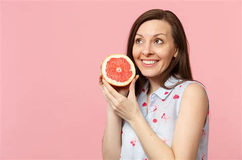 여름 옷에 예쁜 어린 소녀 분홍색 파스텔 벽 배경에 고립 된 신선한 잘 익은 자 몽의 절반 손을 잡고 찾고 사람들은 생생한 라이프 스타일 휴식 휴가 개념입니다 복사 공간을