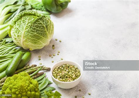 모듬된 그린 톤의 흰색 돌 배경에 원시 유기농 야채 아보카도 양배추 브로콜리 콜리플라워와 트림된 콩 및 분할 완두콩 흰 그릇에