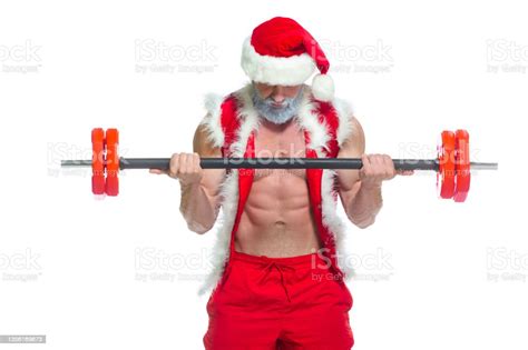 크리스마스 크리스마스 모자와 빨간 반바지를 입고 회색 수염을 가진 강한 근육의 산타 클로스는 흰색 배경에 고립 된 운동을 수행하는 체육관에서 무거운 바벨을 들어 올리고 있다