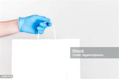 검역 중 물품 배달의 개념 파란 장갑을 낀 젊은 남자는 하얀 바탕에 하얀 종이 봉지를 손에 들고 있다 팬데믹에서 코로나바이러스 2019ncov에 대한 배송 비접촉식 배송