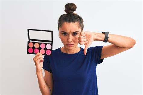 화가 얼굴 엄지 손가락으로 싫어하는 것을 보여주는 부정적인 기호 거부 개념으로 고립 된 흰색 배경 위에 서있는 메이크업을 들고있는 젊은 아름다운 여성 갈색 머리에 대한 스톡