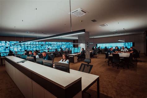 Group Of Security Data Center Operators Working In A Cctv Monitoring Room Looking On Multiple