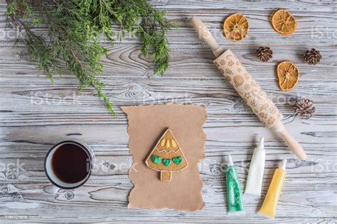 나무 회색 테이블과 공예 용지에 크리스마스 트리의 형태로 꿀 진저 브레드 쿠키를 장식하는 여성 빈 비스킷 진저 브레드 작은 전나무 장식 할 준비 아이싱 베이커리 플랫 레이