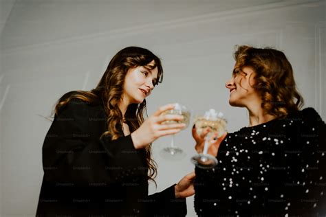 A Couple Of Women Standing Next To Each Other Holding Wine Glasses