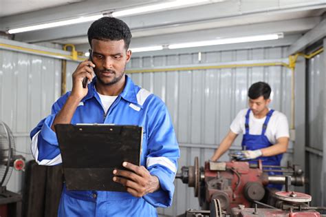 금속 선반 기계를 사용하는 다민족 기술자 정비사는 차고에서 스마트 휴대폰과 클립 보드로 자동차 디스크 브레이크 연마를 작동합니다 유지 보수 자동차 및 검사 차량 부품 개념