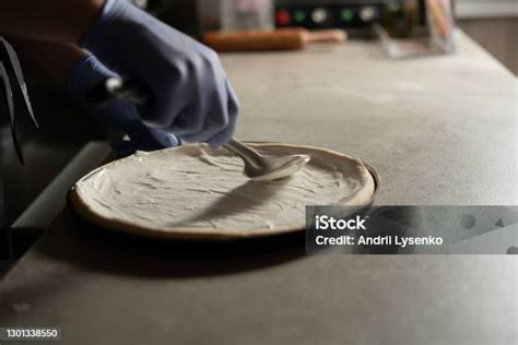 피자 반죽을 준비합니다 고무 장갑을 낀 베이커의 손이 사워 크림 소스를 금속 금형의 피자 반죽 베이스 위에 펼쳐 놓습니다 반죽 주식에 대한 스톡 사진 및 기타 이미지