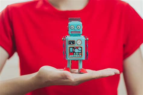 빨간 셔츠를 입은 빈티지 장난감 로봇을 들고 다채로운 디자인과 기능을 보여주는 사람 로봇은 장난기 넘치는 표정을 지으며 향수와 기쁨을 불러일으킵니다 개성 개념에 대한 스톡