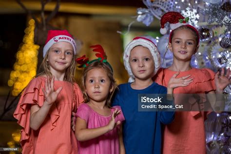 크리스마스 트리 근처에 서있는 산타 모자를 쓰고 손을 흔들고 인사를하는 행복한 귀여운 어린 아이들 메리 크리스마스와 해피 홀리데이 12월에 대한 스톡 사진 및 기타 이미지