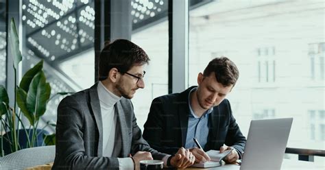 두 사업가가 새로운 기회에 대해 이야기하는 큰 창문 근처 책상에 노트북을 놓고 프로젝트를 계획하고 사업 제안을 고려하고 있습니다 사진 Unsplash의 점심 모임 이미지