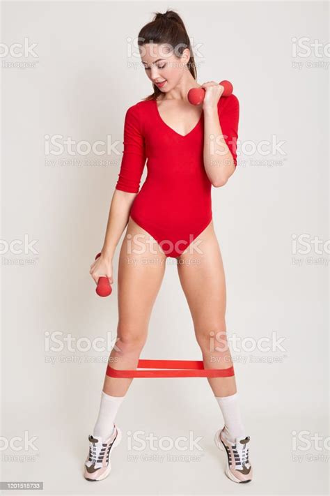 화려한 성인 스포츠 여자 흰색 배경 위에 고립 된 Dambbells와 피트 니스를 하 고 스포티 한 여성 레드 콤비 드레스와 흰색 운동화를 입고 카메라를 직접 보고 건강한