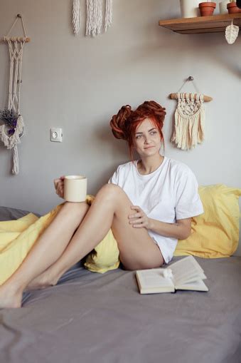 아침에 침실에서 침대에 두려움을 가진 아주 예쁜 빨간 머리 소녀 여성스럽고 부드러운 소녀 침대에서 아침 식사를하는 소녀는 커피 한 잔을 들고 책을 읽습니다 20 24세에