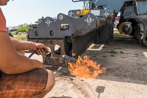 남자도로 건설 및 작품을 복구 하는 동안 아스팔트 포장 재료 기계에 오래 된 건조 아스팔트를 녹기 위하여 가스 실린더에서 화재를 사용 합니다 작업에 대 한 장비의 준비입니다