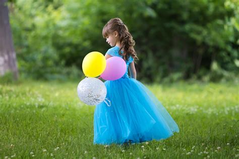 프로필 예쁜 작은 금발 긴 머리 소녀의 전체 길이 초상화 는 흐린 녹색 나무 배경에 피는 필드에 서 화려한 풍선 긴 파란색 드레스 행복 한 어린 시절 개념입니다 결혼식에