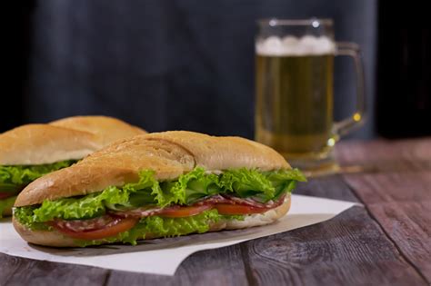 어두운 나무 배경에 소시지 치즈 베이컨 토마토 양상추 오이 및 양파가 있는 두 개의 신선한 잠수함 샌드위치 맥주 머그잔 대형에 대한 스톡 사진 및 기타 이미지 Istock