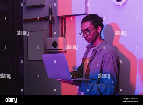 Young African American Programmer In Eyeglasses Using Laptop In Data Center In Neon Light Stock
