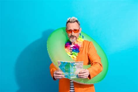 강렬한 오렌지색 양복을 입고 여름 액세서리를 착용한 카리스마 넘치는 중년 남자가 파란색 배경에서 목적지 지도를 탐험하고 있습니다 45 49세에 대한 스톡 사진 및 기타