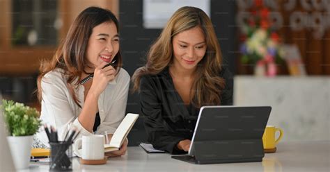 두 명의 여성 비즈니스 기업가가 현대 사무실의 회의실 테이블에서 태블릿을 사용하여 함께 일하면서 웃고 있습니다 사진 Unsplash의 태국 이미지