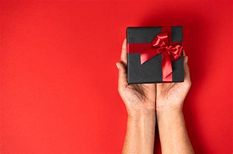 빨간 배경에 빨간 새틴 리본이 달린 검은 선물 상자를 들고 있는 노인 여성의 손 발렌타인 데이 여성의 날 어머니의 날 공간을