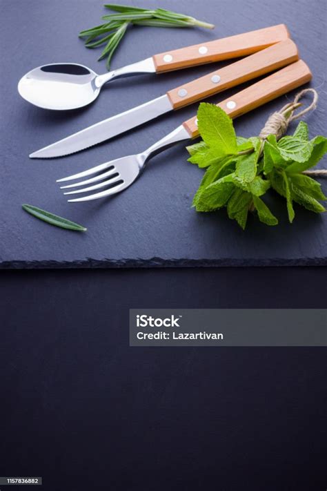 칼 세트입니다 칼 숟가락 슬레이트 돌에 포크 로즈마리와 민트가 있는 크립토클러 검은 색 배경입니다 공간을 복사합니다 맨 위 보기