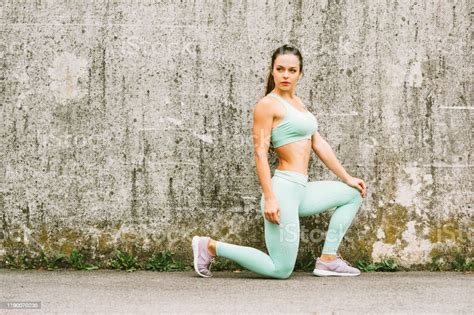 녹색 액티브 웨어를 입고 다리를 스트레칭 하는 젊은 아름 다운 피트 여자 회색 도시 벽 배경 옆에 포즈 선수 모델 스포츠 패션의 야외 초상화 거리에 대한 스톡 사진 및 기타