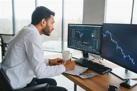 Young Indian Business Man Trader Looking At Computer Screen With Trading Charts Reflecting In
