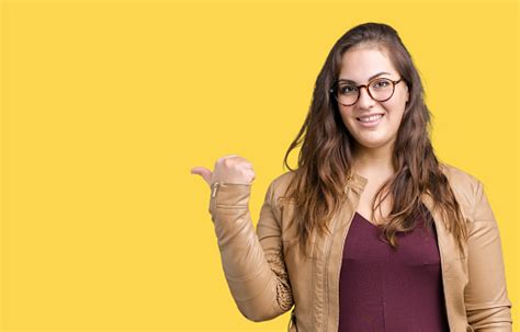 격리 된 배경에 생기고 엄지 측면 가리키는 행복 한 얼굴로 웃 고 드레스와 가죽 재킷을 입고 아름 다운 플러스 크기 젊은 여자 가리키기에 대한 스톡 사진 및 기타 이미지