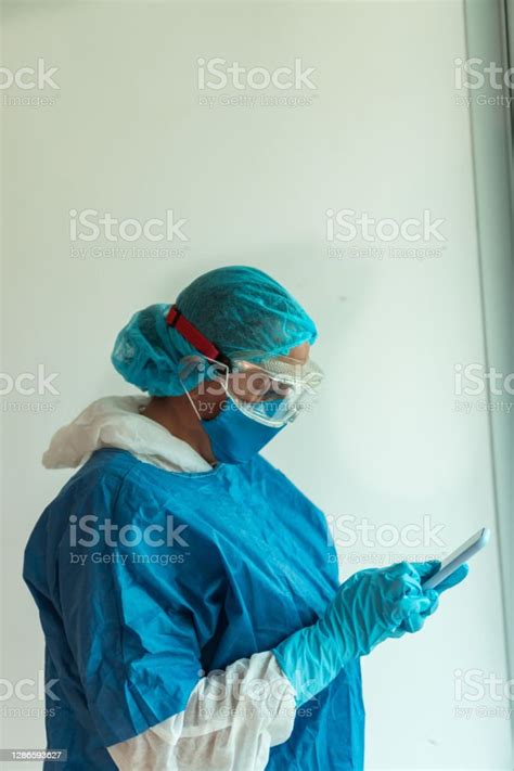 파란 유니폼을 입은 젊고 진지한 의사와 병원에서 휴대 전화와 라텍스 장갑을 착용하고 일하는 의료 용 마스크 건강관리와 의술에 대한 스톡 사진 및 기타 이미지 Istock