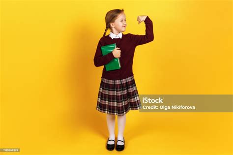 노란색 배경에 유니폼을 입은 전체 길이 여학생 어린 소녀는 손의 힘을 보여주고 책을 들고 전신에 대한 스톡 사진 및 기타 이미지 전신 초등학생 개념 Istock