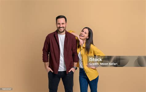 남자친구의 어깨에 손을 얹고 웃으며 카메라를 바라보는 쾌활한 젊은 여자친구 베이지색 배경에 황홀하게 서 있는 행복한 젊은 커플 남자에 대한 스톡 사진 및 기타 이미지