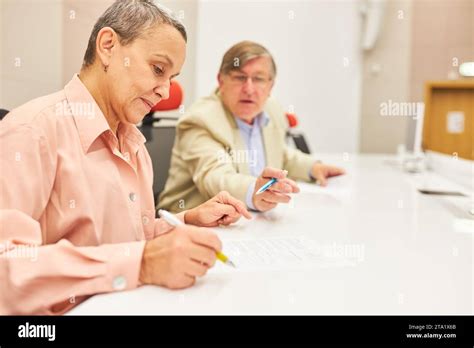 mature female speaker writing in document while sitting by colleague at