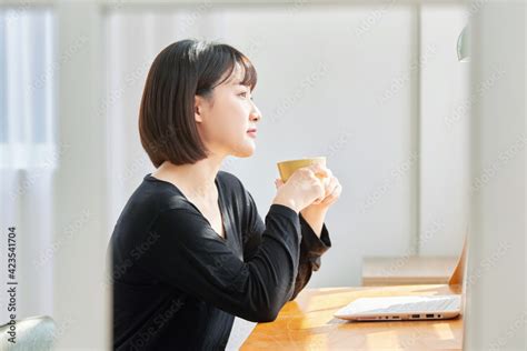 햇살이 비추는 창가 앞 책상에 앉아서 커피 또는 차를 마신다 컴퓨터를 보며 생각 일 대화 온라인 쇼핑 웹서핑을 한다 Stock Foto Adobe Stock