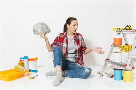 달러 현금 돈의 충격 보유 번들에 여자 흰색 배경에 고립 된 재건축 아파트에 대 한 악기와 함께 바닥에 앉아 있다 벽지 도구를 붙이기 위한 액세서리 집 수리의 개념 개선에