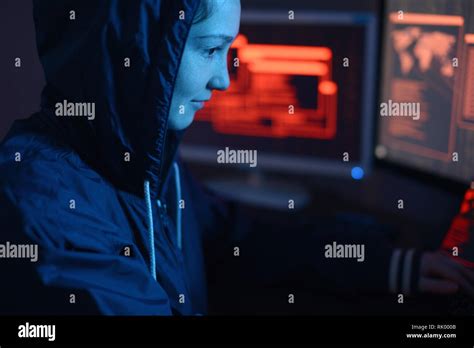 girl hacker in a hood typing program code while committing a cybercrime