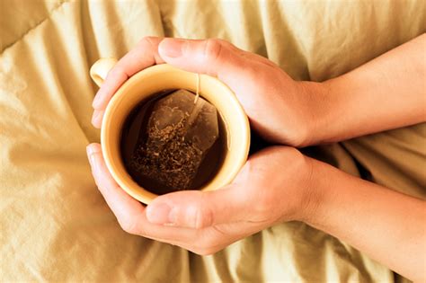 노란 침대 이불에 티백을 곁들인 차 한 잔을 마시는 여성의 손 스며든에 대한 스톡 사진 및 기타 이미지 스며든 가정 생활 노랑 Istock