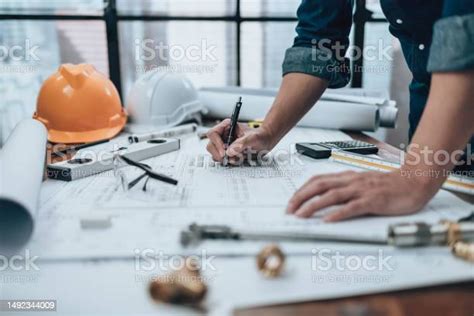 사무실 책상과 계산기 삼각형 눈금자 안전 안경 나침반 블루프린트의 버니어 캘리퍼에서 도면 검사 및 쓰기로 작업하는 엔지니어링 엔지니어 건축가 산업 및 공장 개념 청사진에